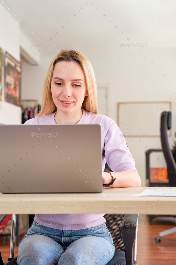 Vertical Eye Level Shot Of Young Blonde Caucasian Girl Working With A Laptop In An Office Stock
